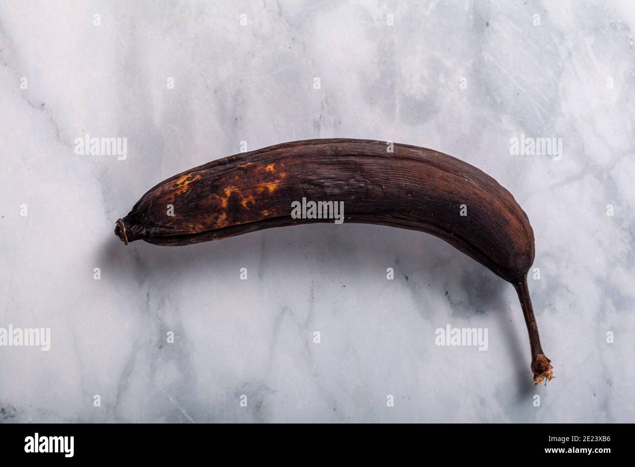 Flat lay image of a banana in its skin. The peel is covered with dark ...