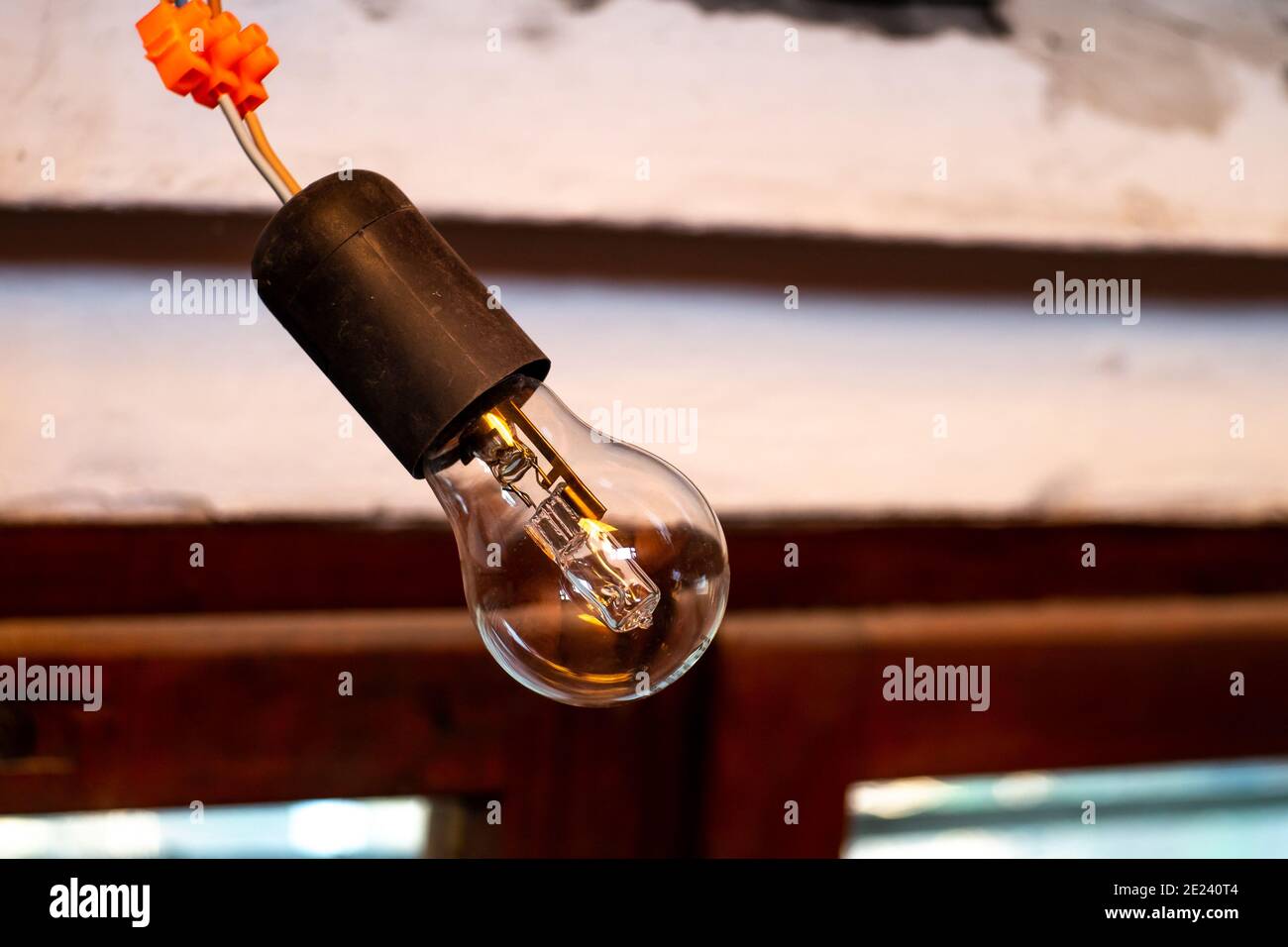 Closeup of a light bulb hanging from wires on a wall with a blurry ...