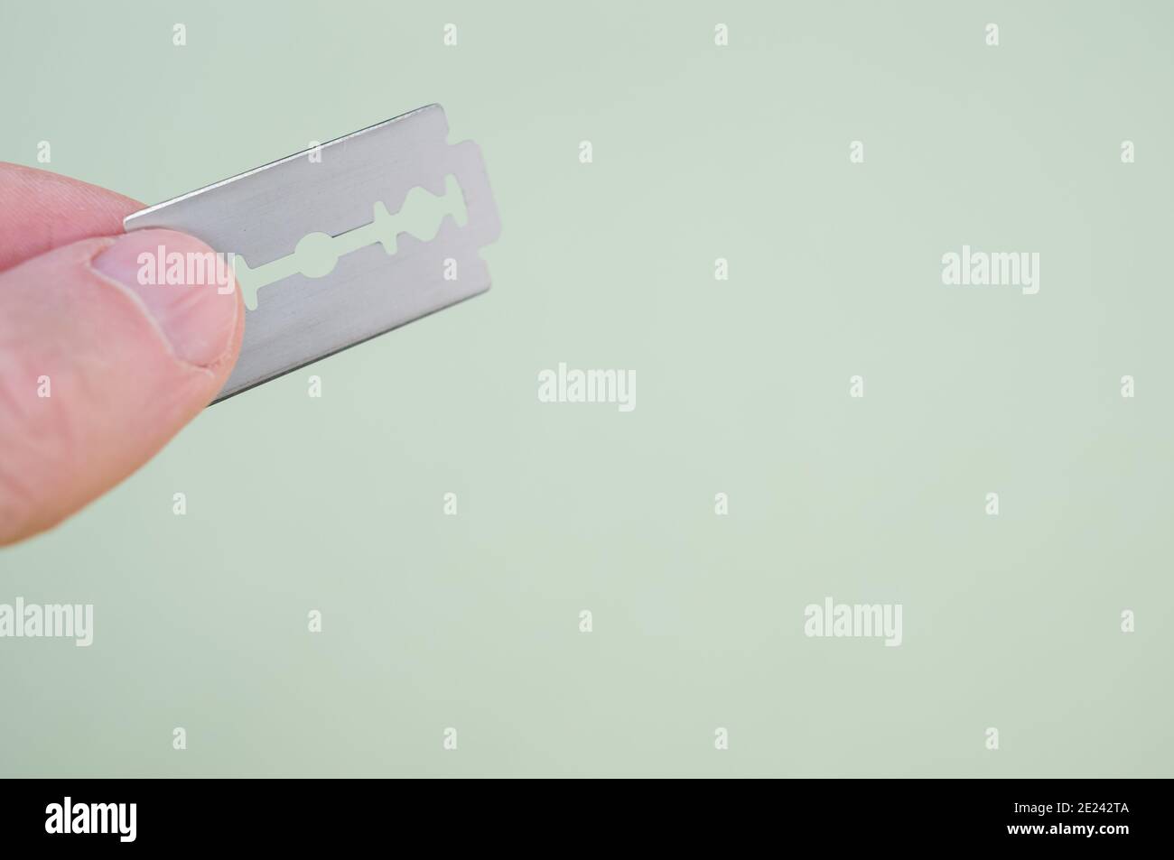 Closeup shot of a hand holding blade isolated on light green background ...