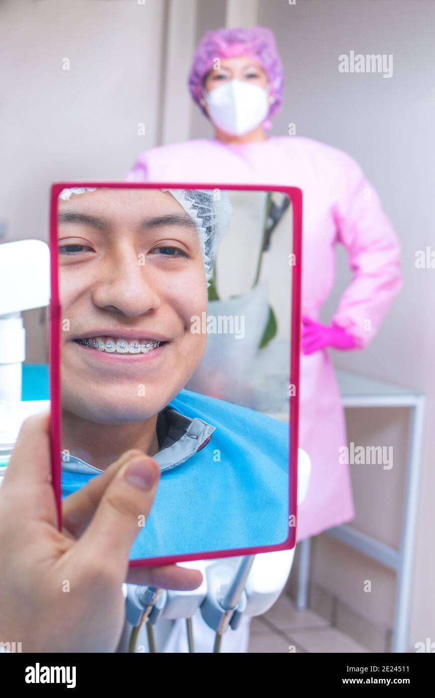 Happy patient in dentistry with teeth brackets looking in the mirror ...