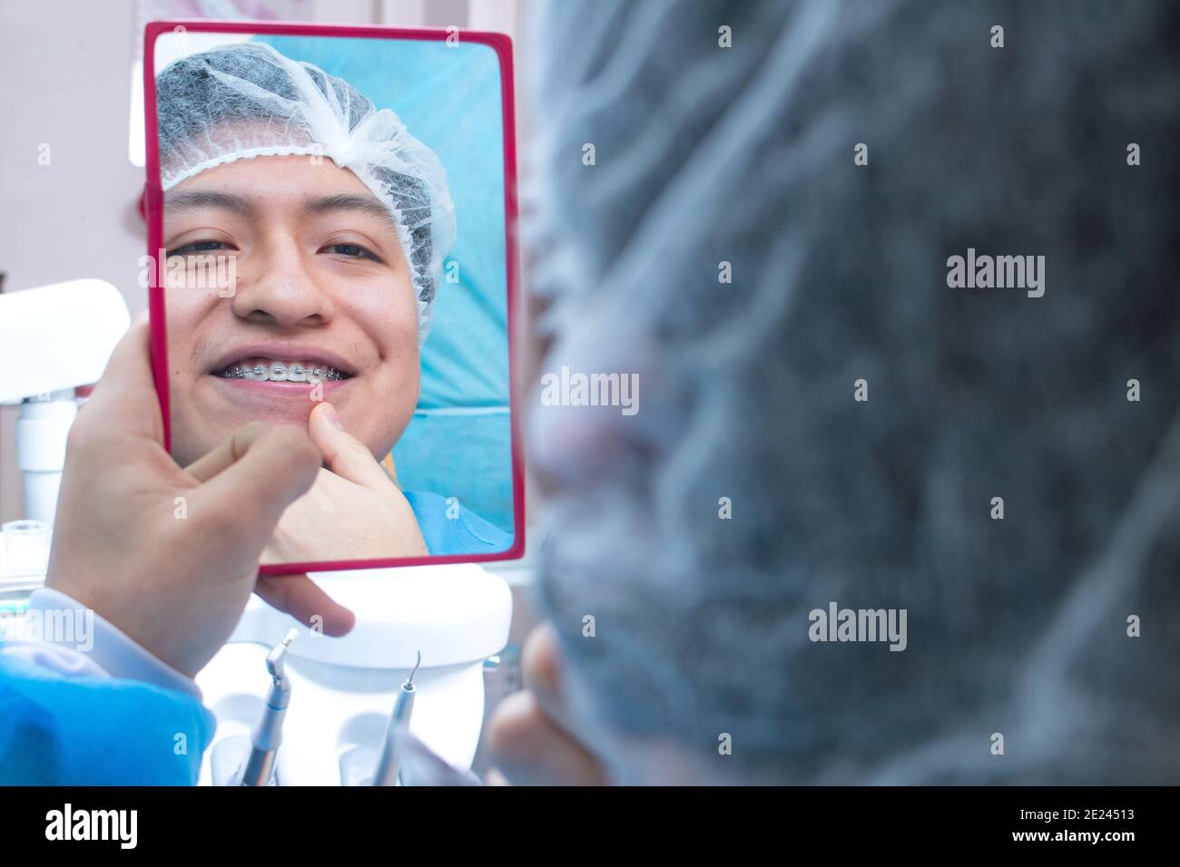 Happy patient in dentistry with teeth brackets looking in the mirror ...
