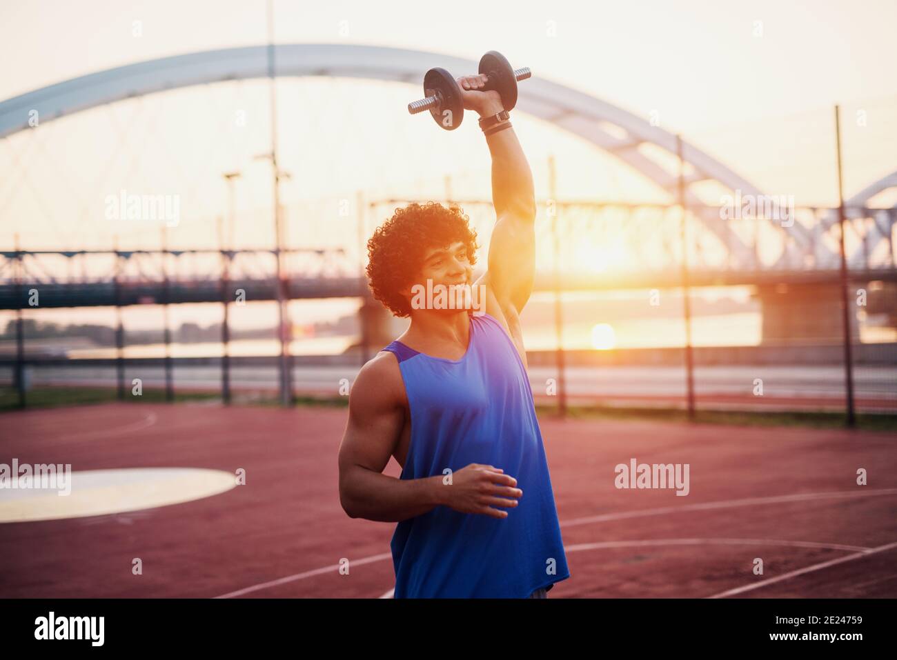 Young sporty fit man holding weight in his arm . Outside early morning ...