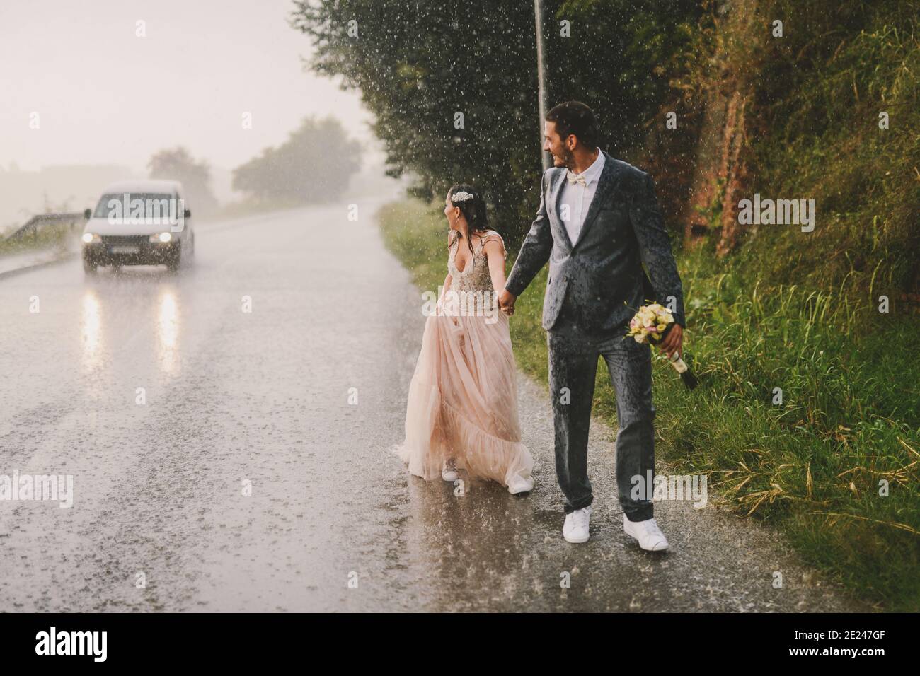 Totally wet just married couple walking on rain by drive road. Watching ...