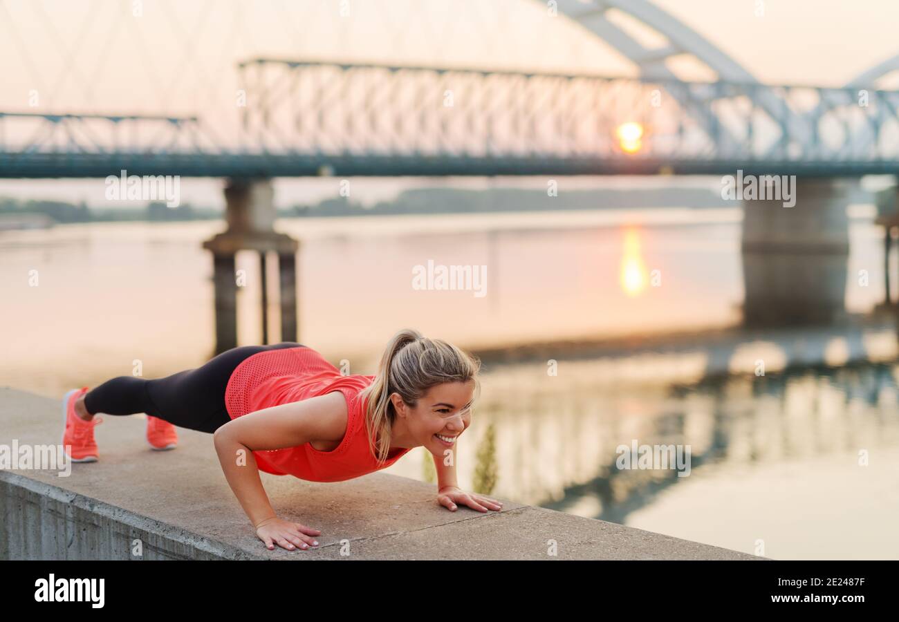 Strong fit blond girl doing push ups outside. Early summer morning ...