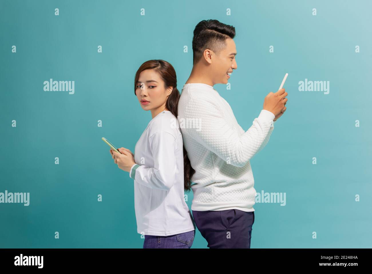 Asian girl and smile guy standing back to back, using mobile phones ...