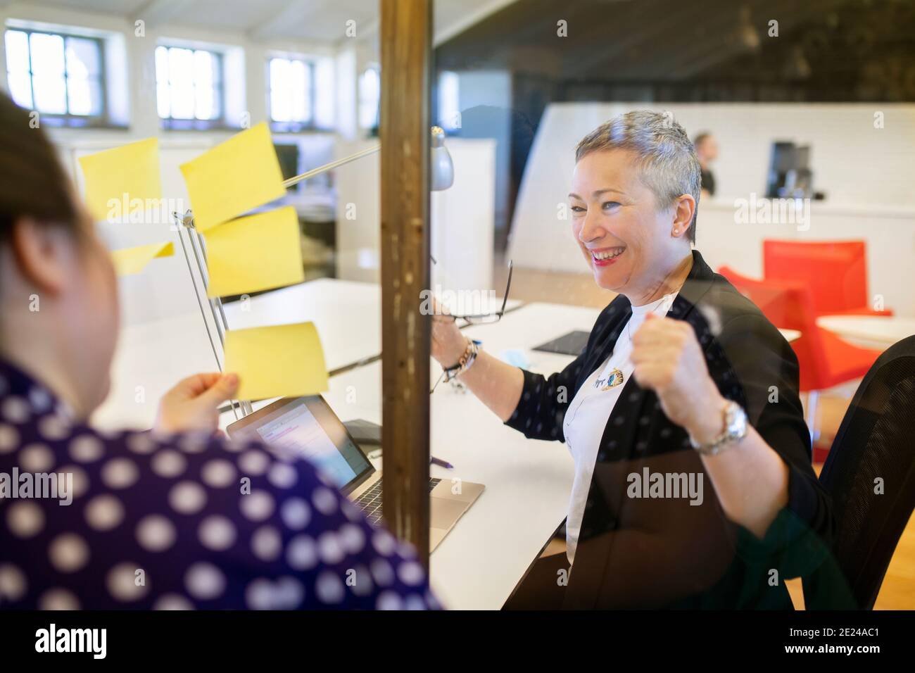 Female office workers communicating through sneeze guard Stock Photo ...