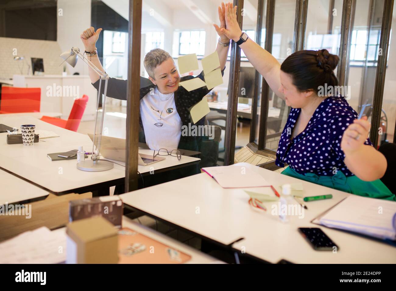 Female office workers giving high five through sneeze guard Stock Photo ...