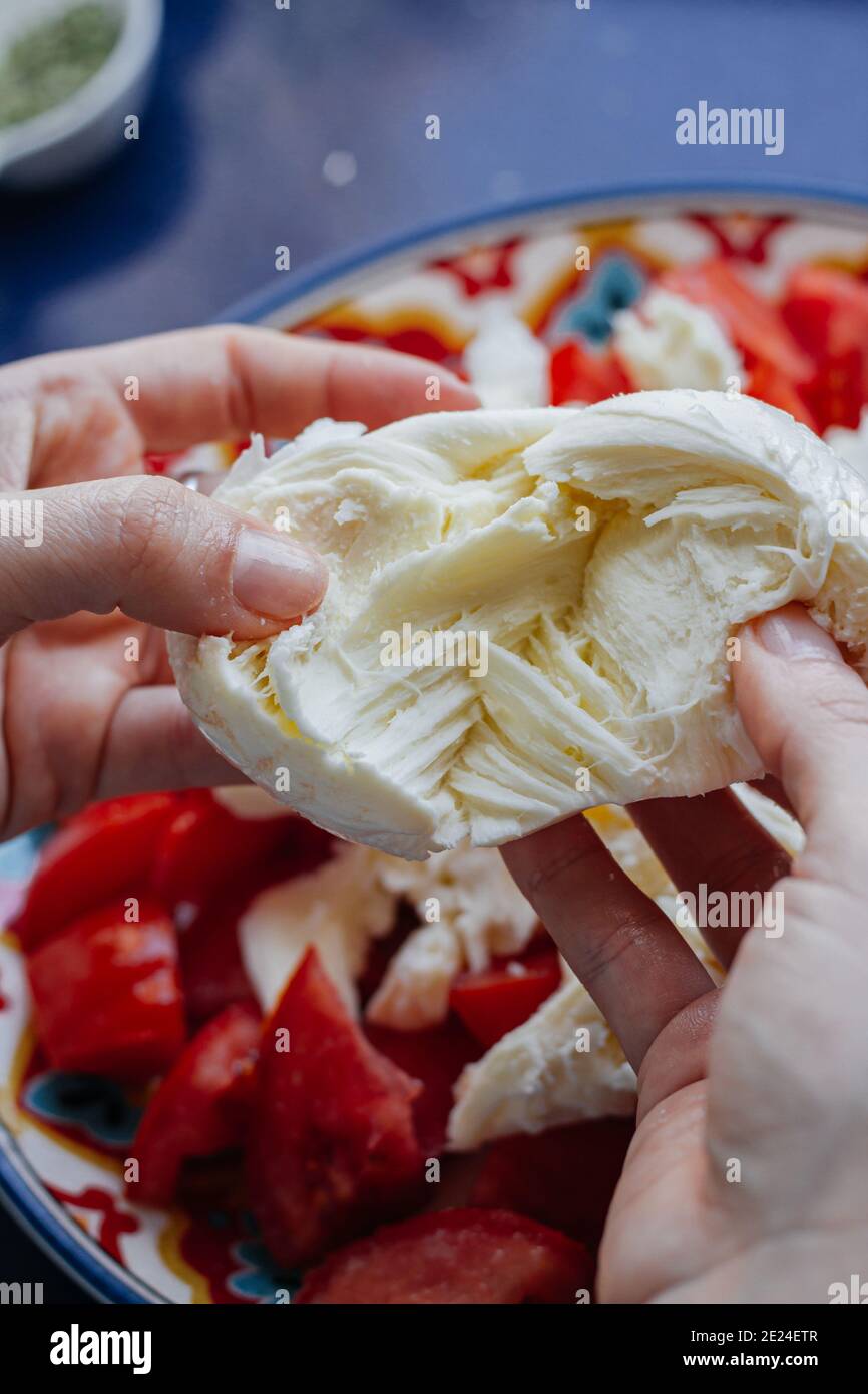 Hand crumbling a mozzarella cheese ball over some tomatoes. Caprese ...
