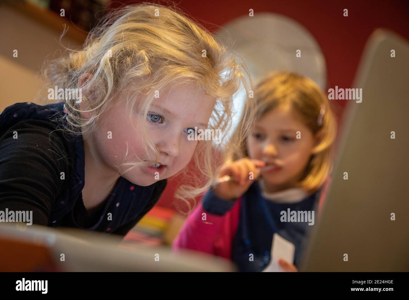 A girl of 3 learning from her laptop computer at home. Her 5 year old ...
