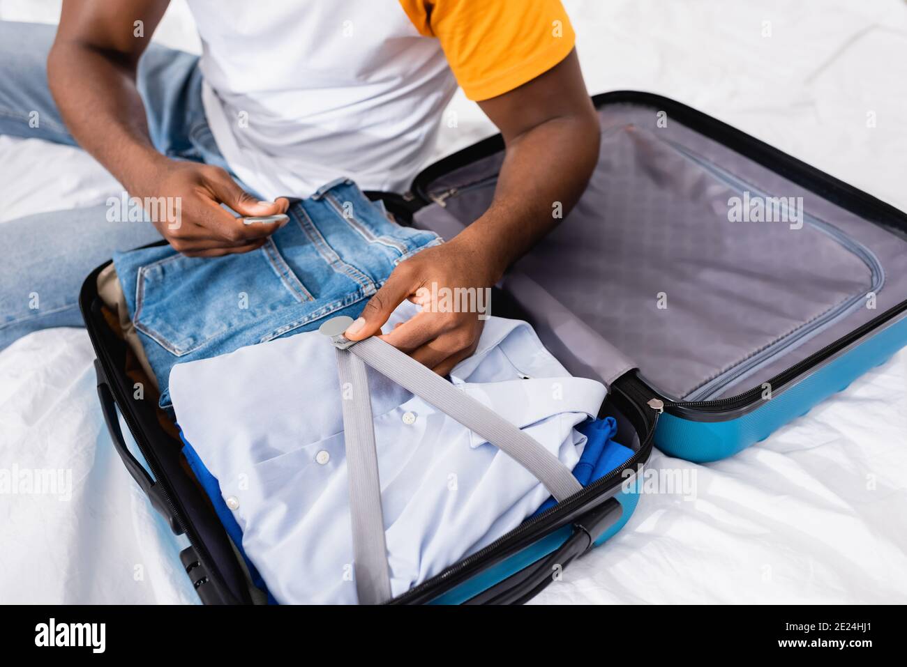 Cropped view of african american man gathering suitcase with clothes on ...