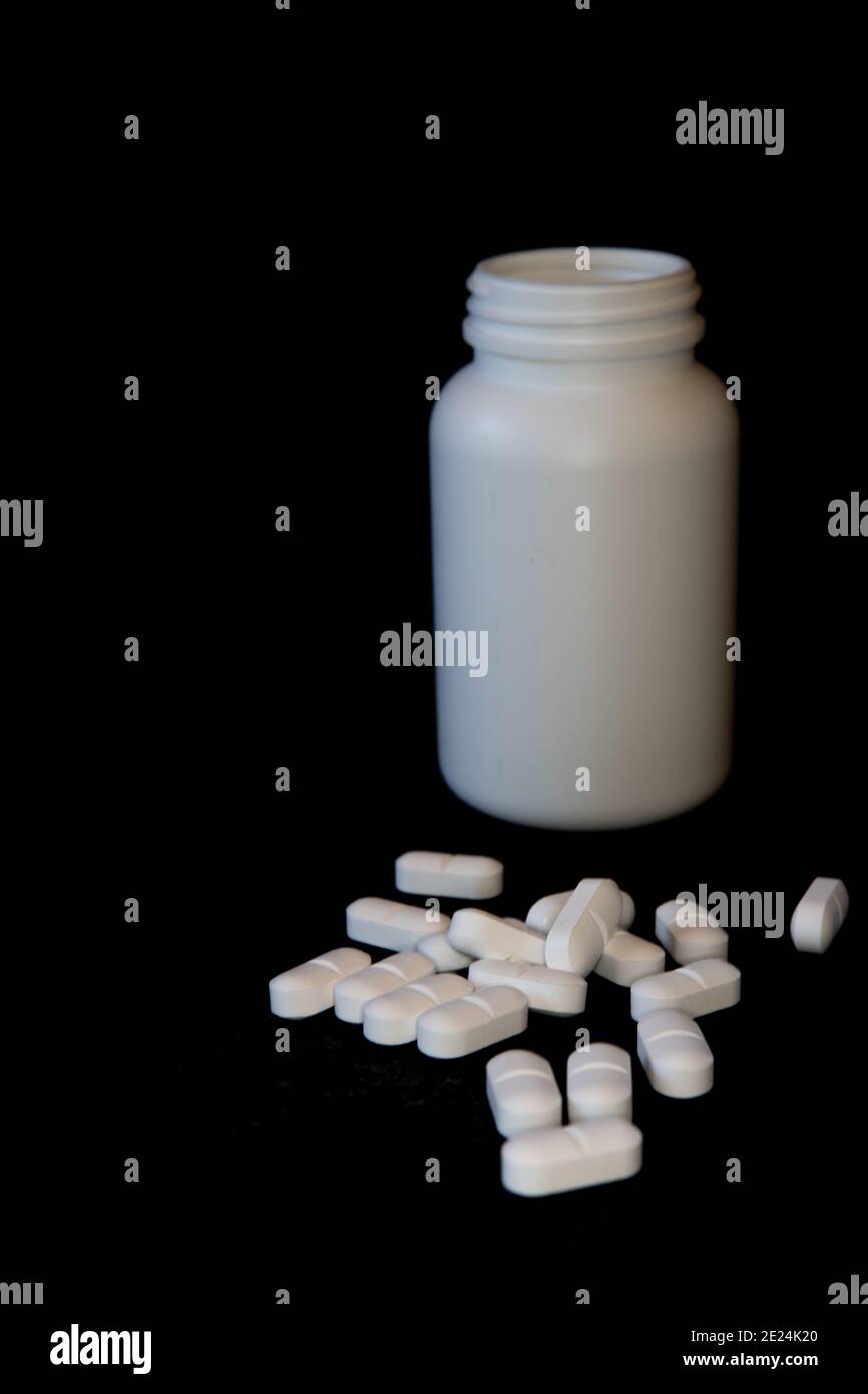 Vertical closeup of medicine tablets and their bottle on a black ...