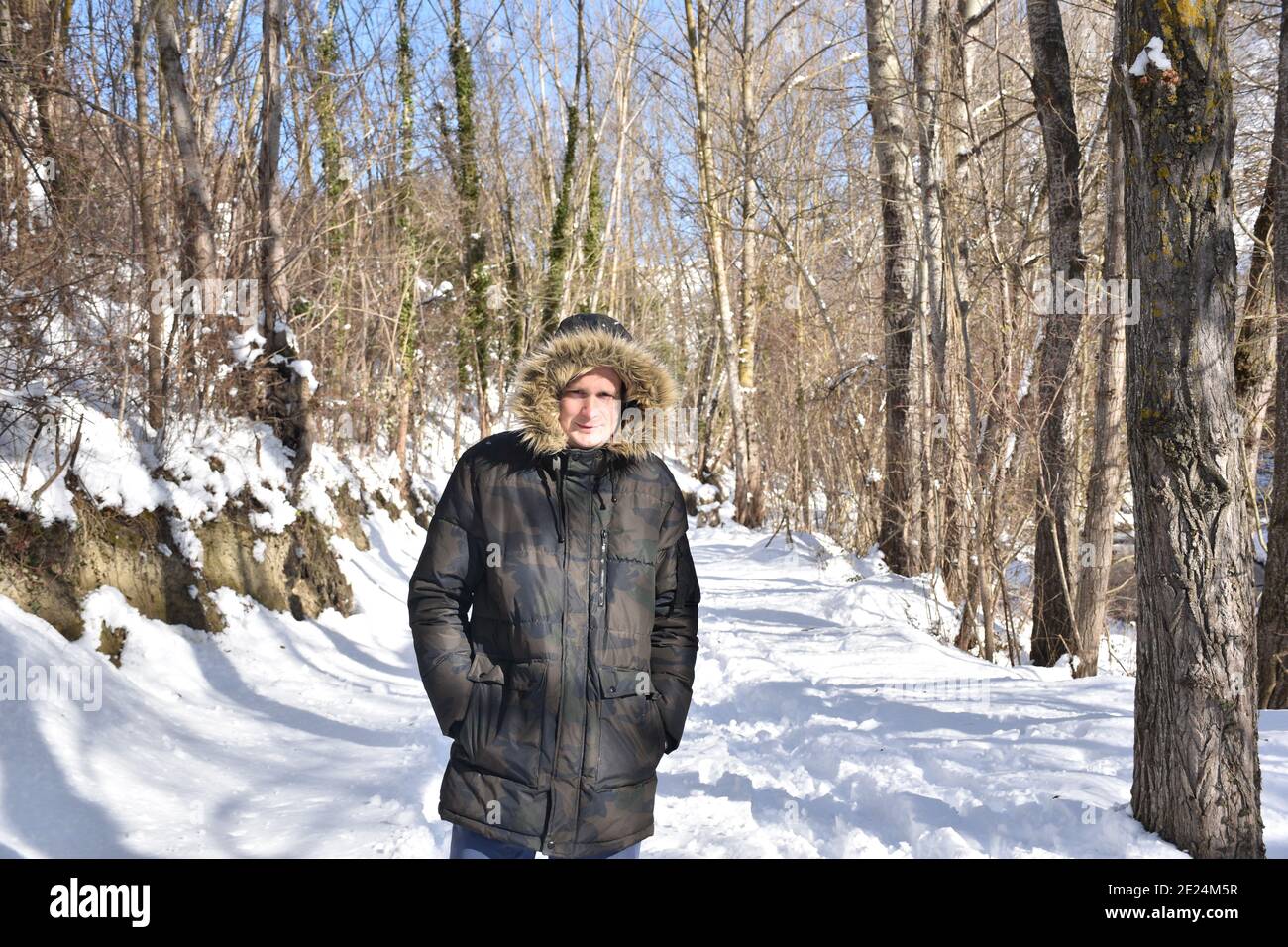 A sunny and snowy day, a man with a military-colored jacket and hood in ...