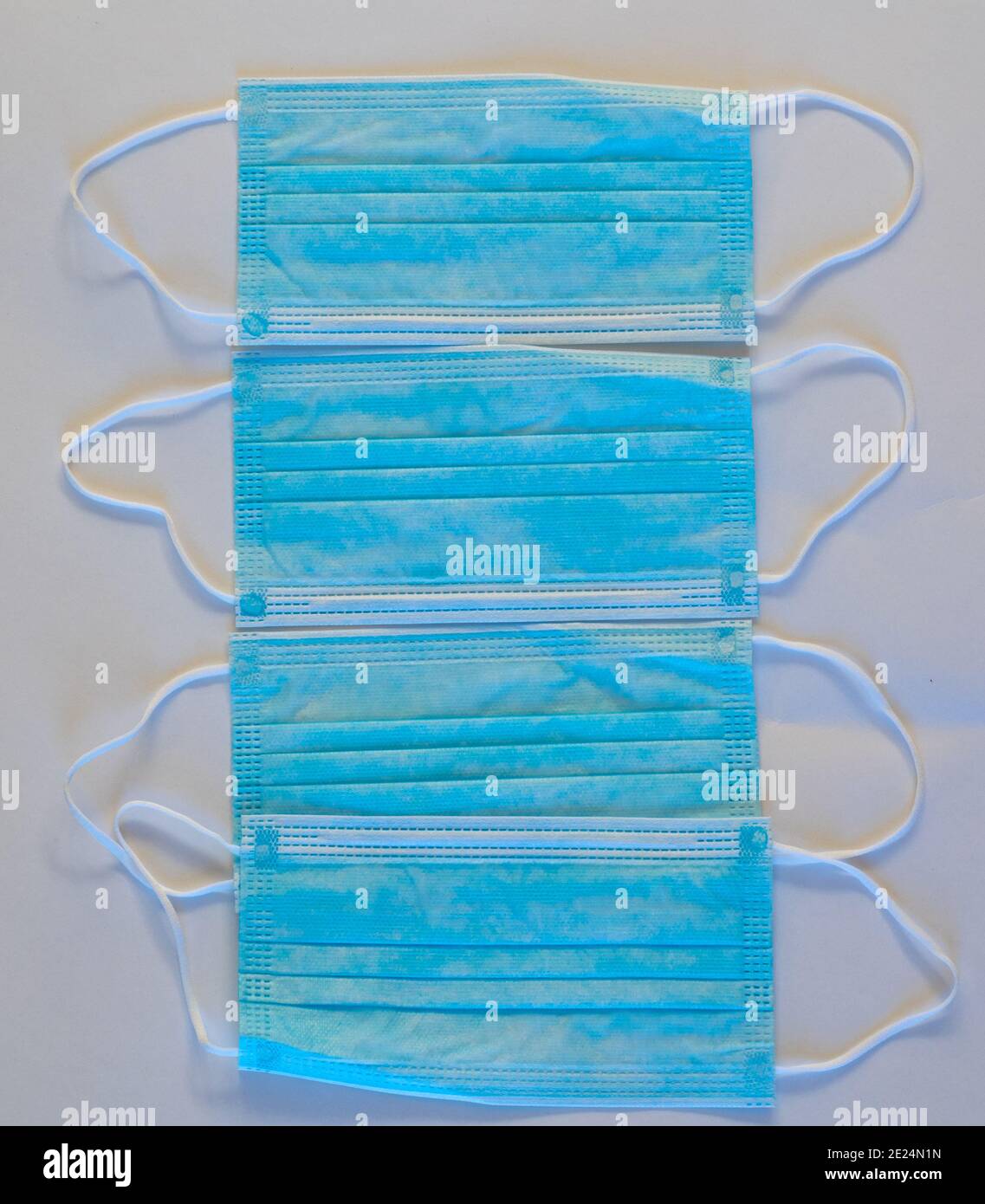 Overhead shot of four light blue medical masks placed next to each ...