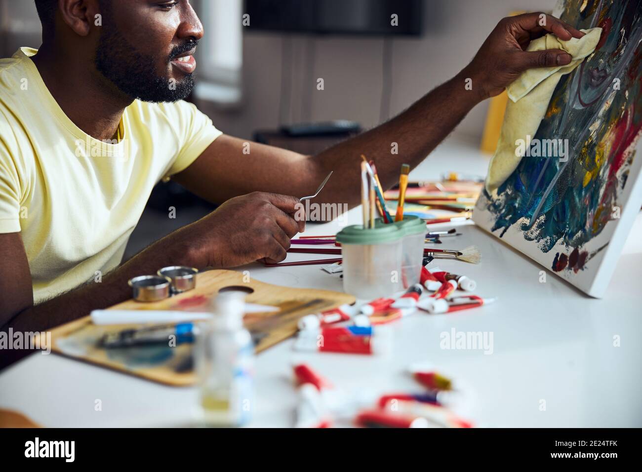 Multiracial artist touching a painting with a rag Stock Photo - Alamy
