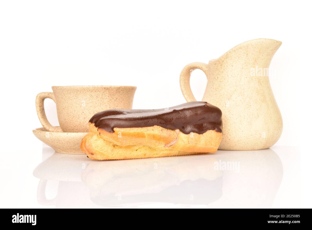 One chocolate eclair with ceramic saucer, cup and milk jug, close-up ...