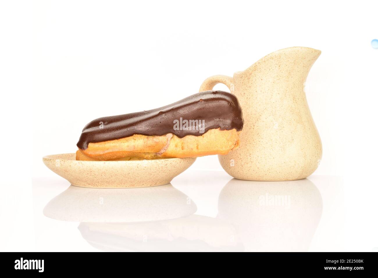 One chocolate eclair on a ceramic saucer with a ceramic milk jug, close ...