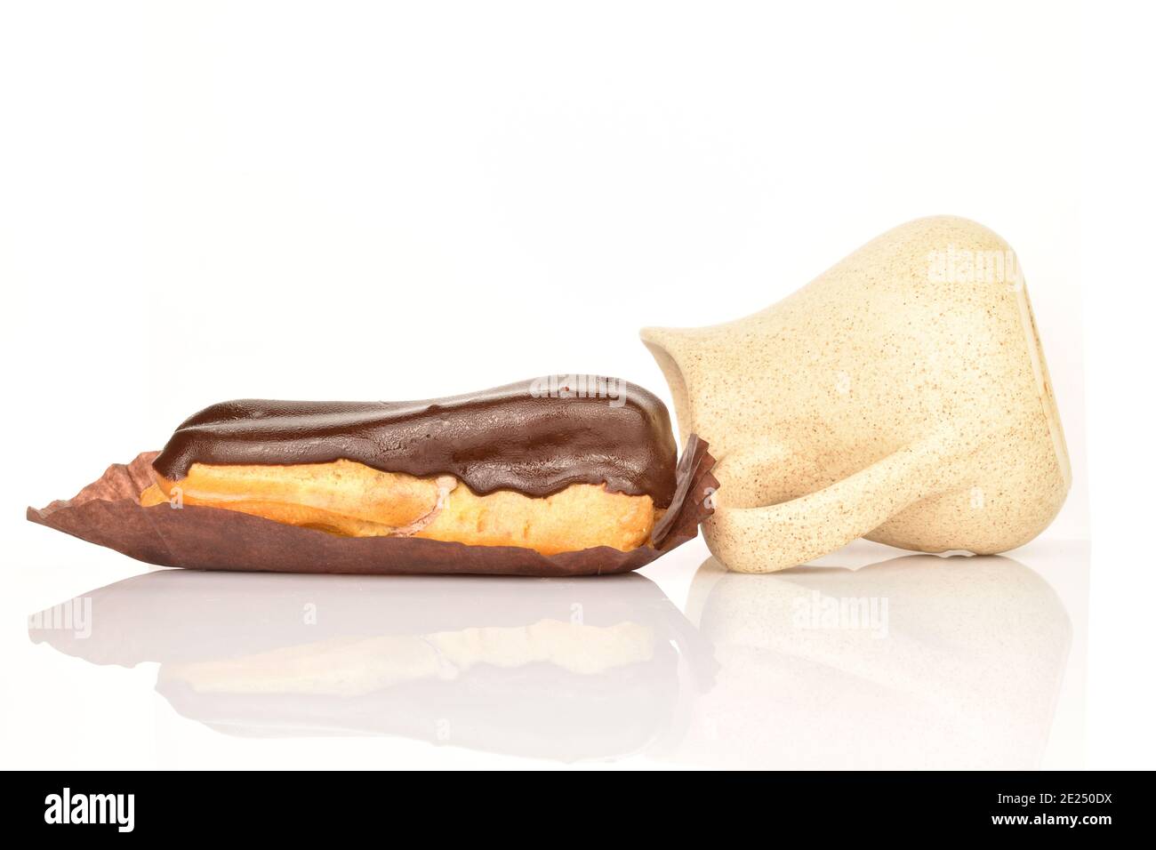 One chocolate eclair with a ceramic milk jug, close-up, isolated on ...