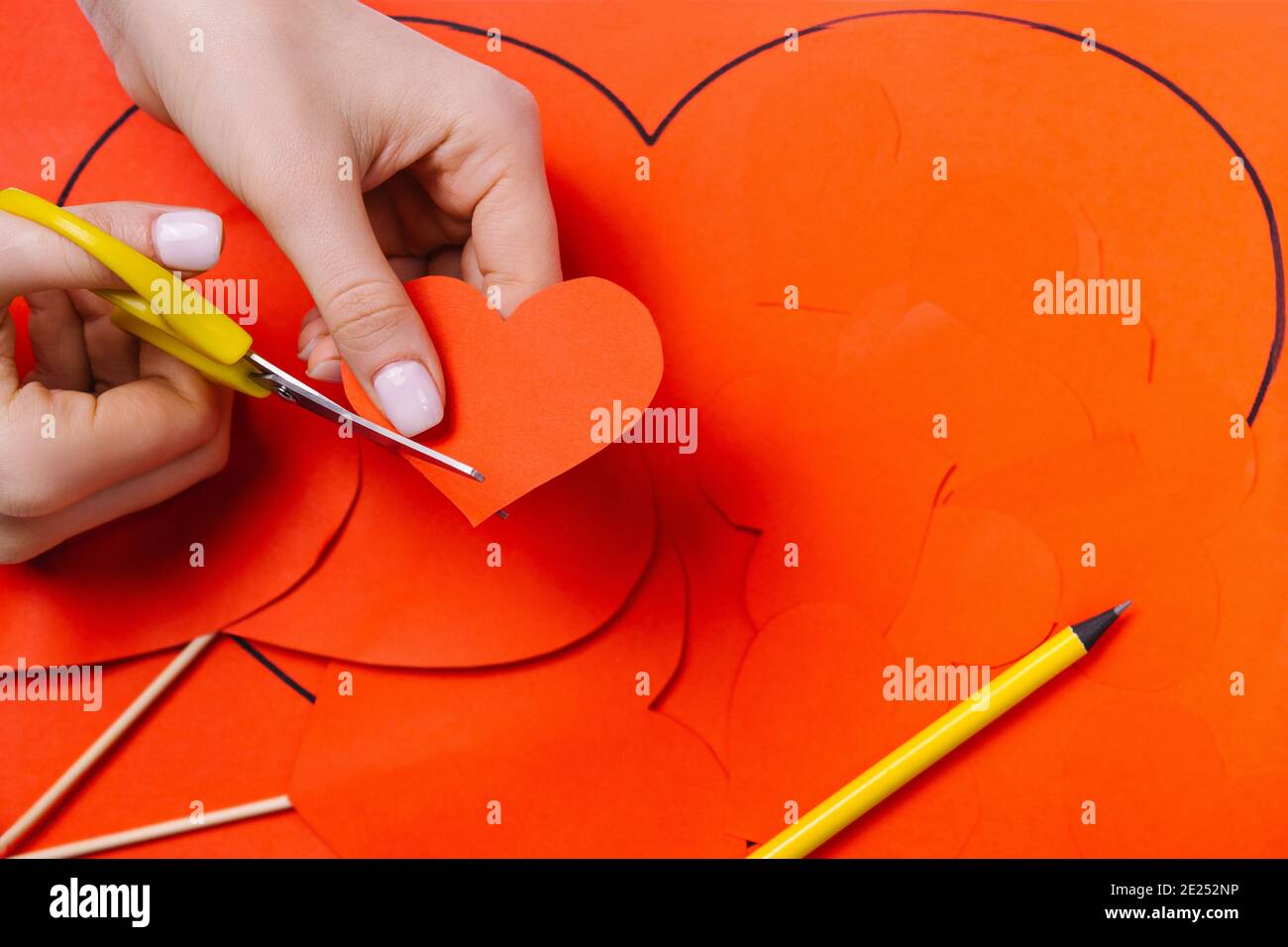 Women's hands cut out a red heart on the background of a pencil and a ...