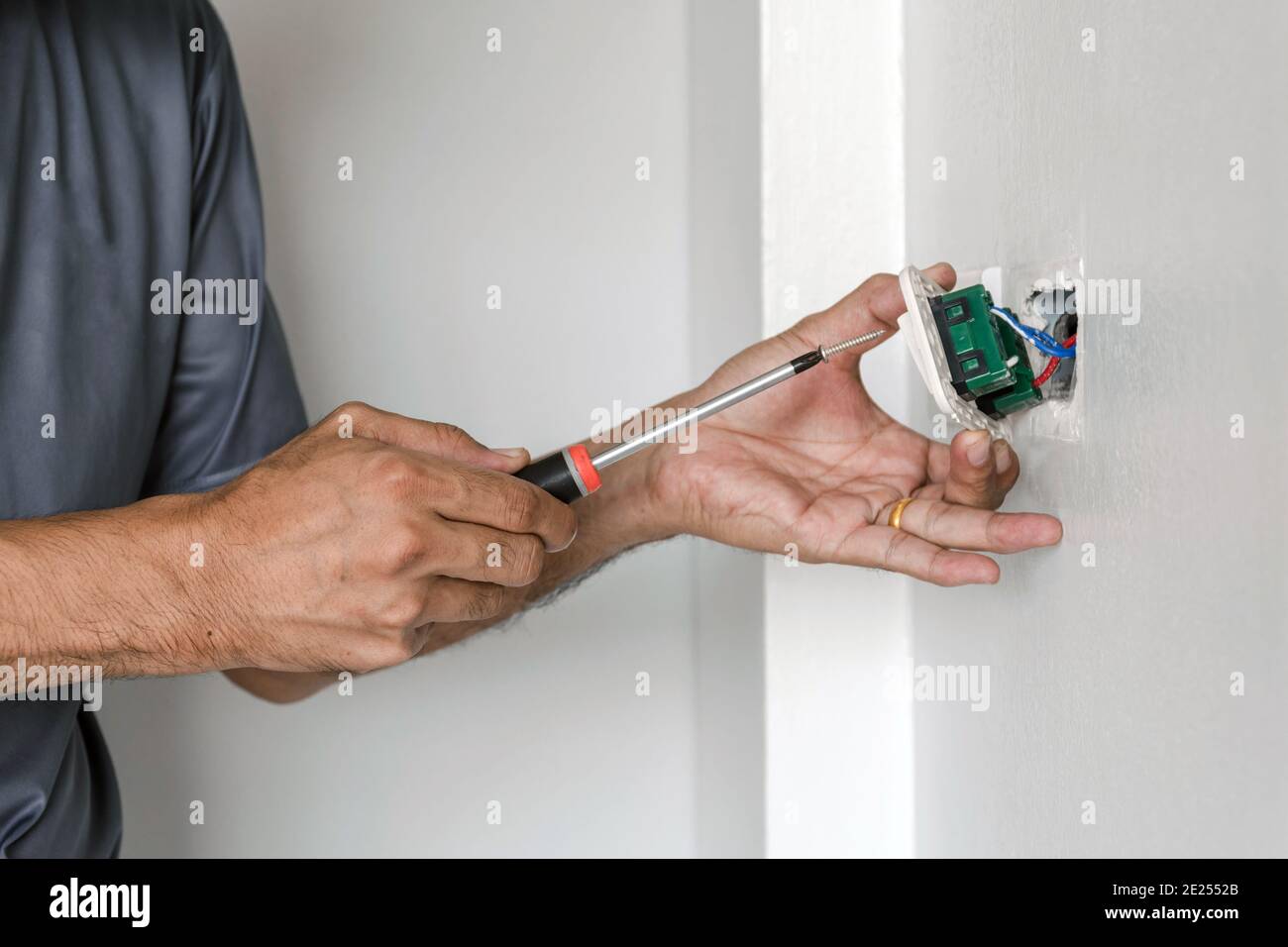 The electrician is using a screwdriver to attach the power cord to the ...