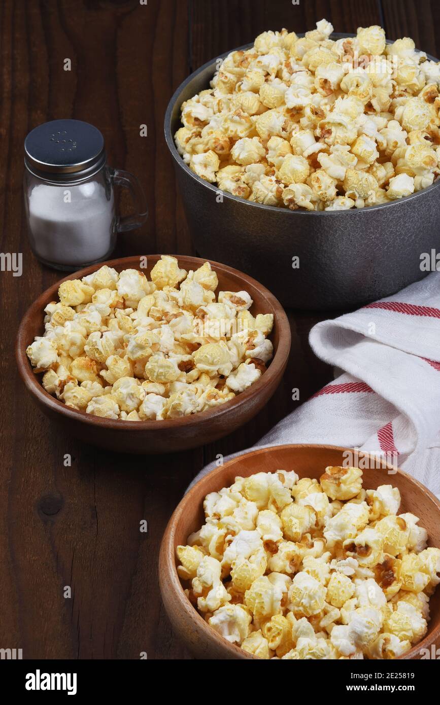 A pot of fresh popped popcorn and two bowls on a rustic wood table with ...