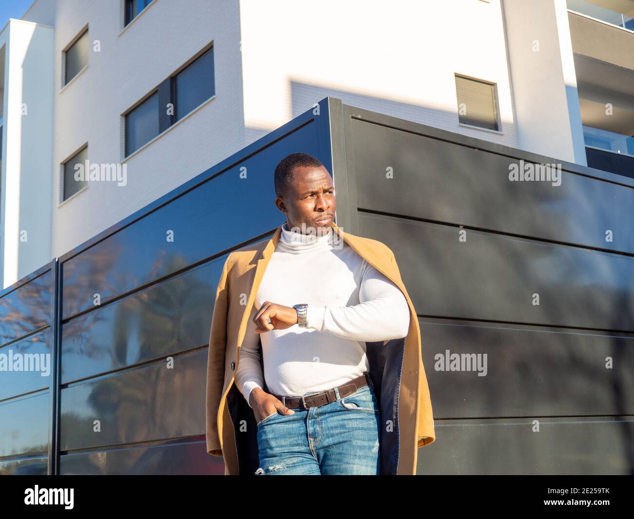 Stylish African male showing his watch on the wrist while leaning on a ...