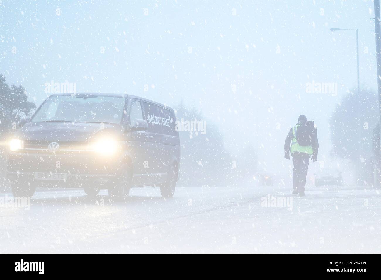 Rear view of male pedestrian walking on icy pavement as heavy snow is ...
