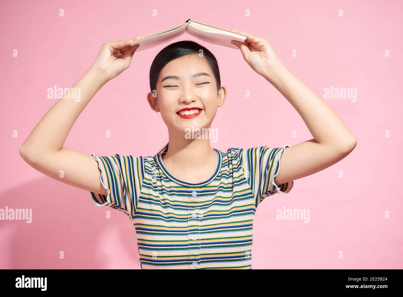 Close-up of a cheerful asian female student holding book over her head ...