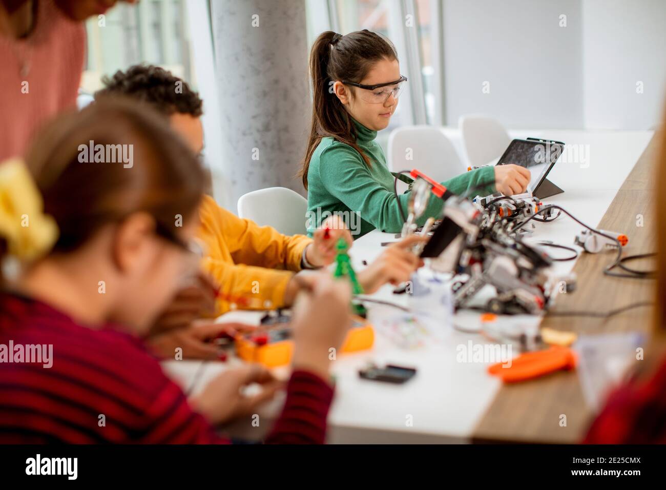 Smily African American female science teacher with group of kids programming electric toys and ...