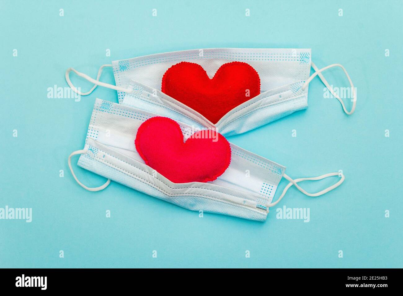Red and pink hearts with medical protection masks on light blue ...
