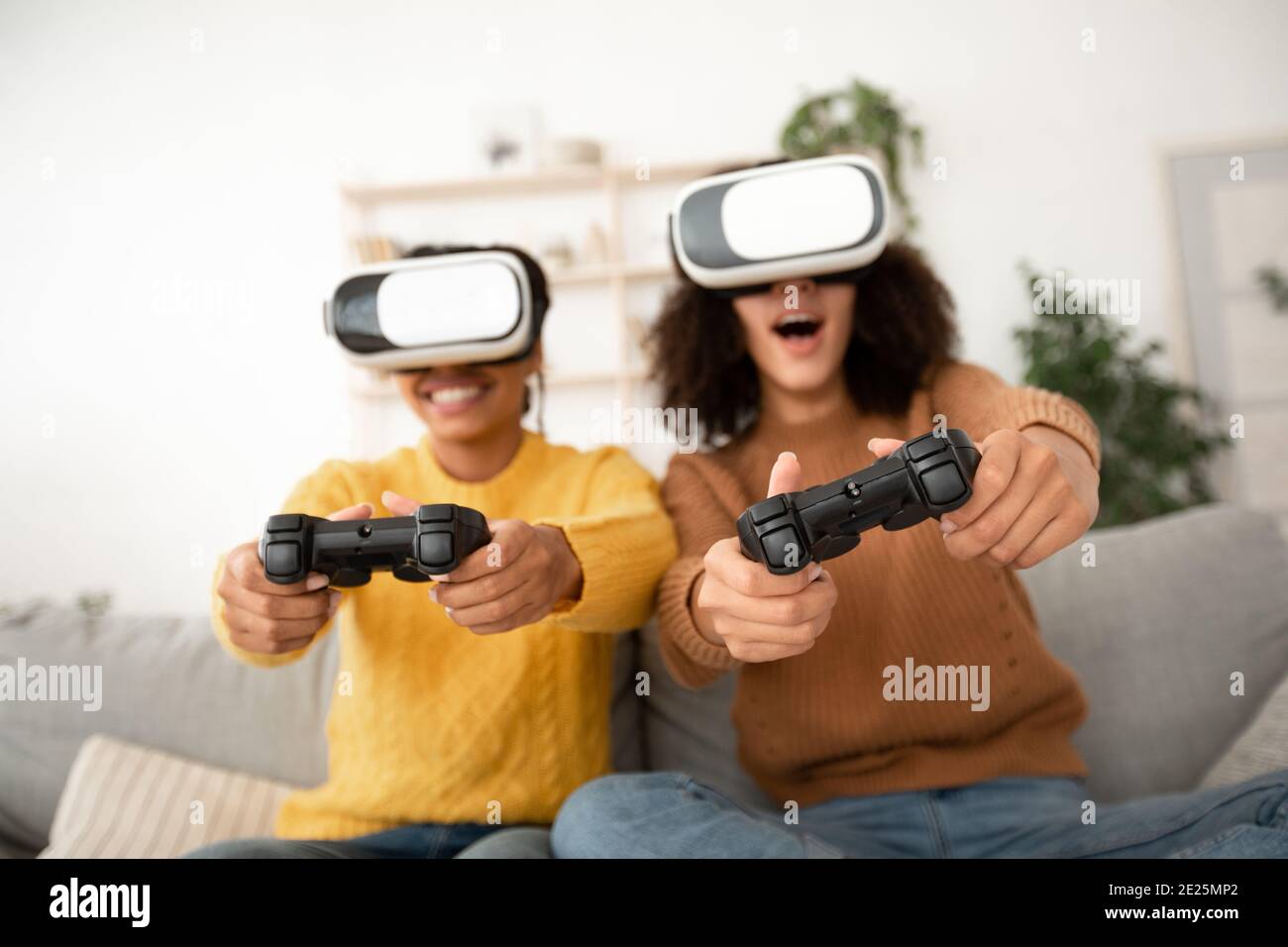 Amazed millennial funny african american sisters with joysticks in vr ...