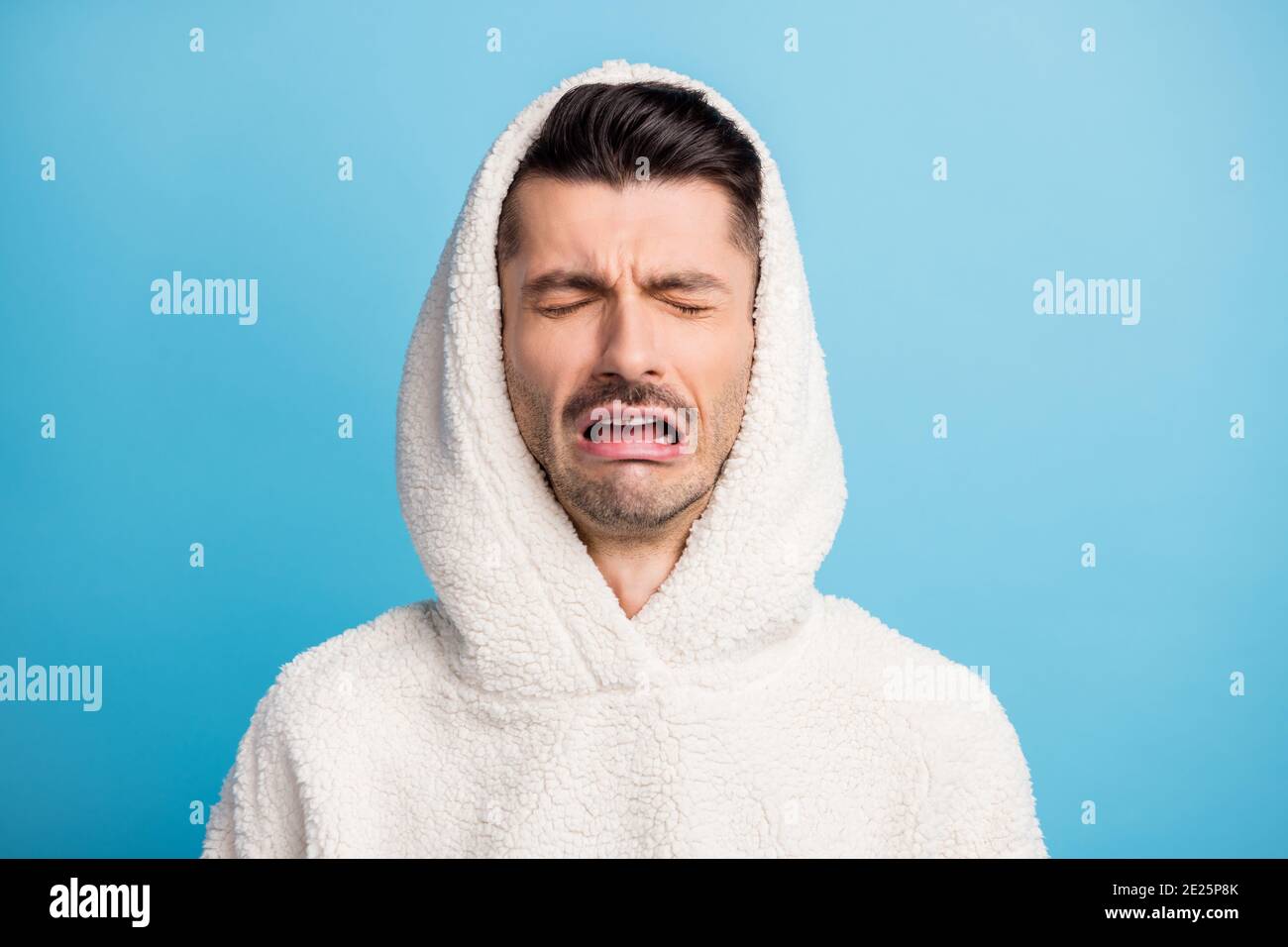 Photo portrait of crying guy wearing wool hood isolated on pastel blue ...