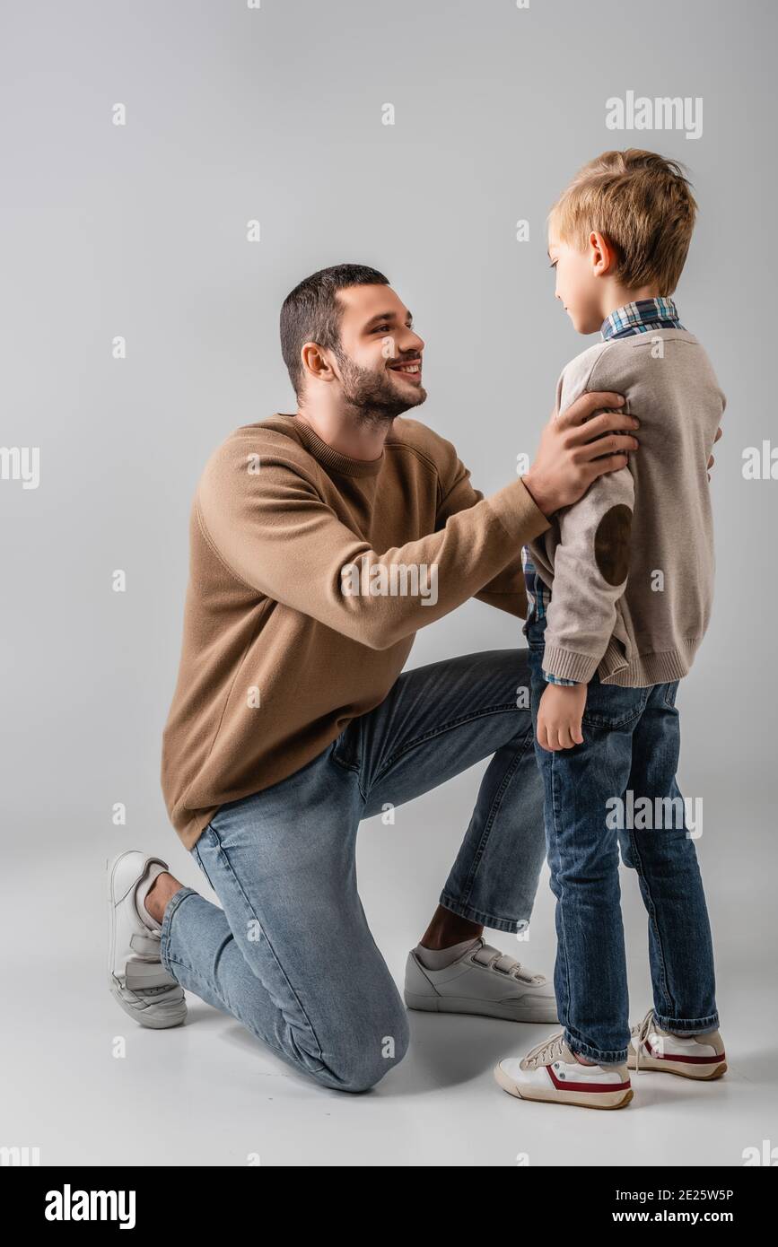 happy man in casual clothes touching son while talking to him on grey ...