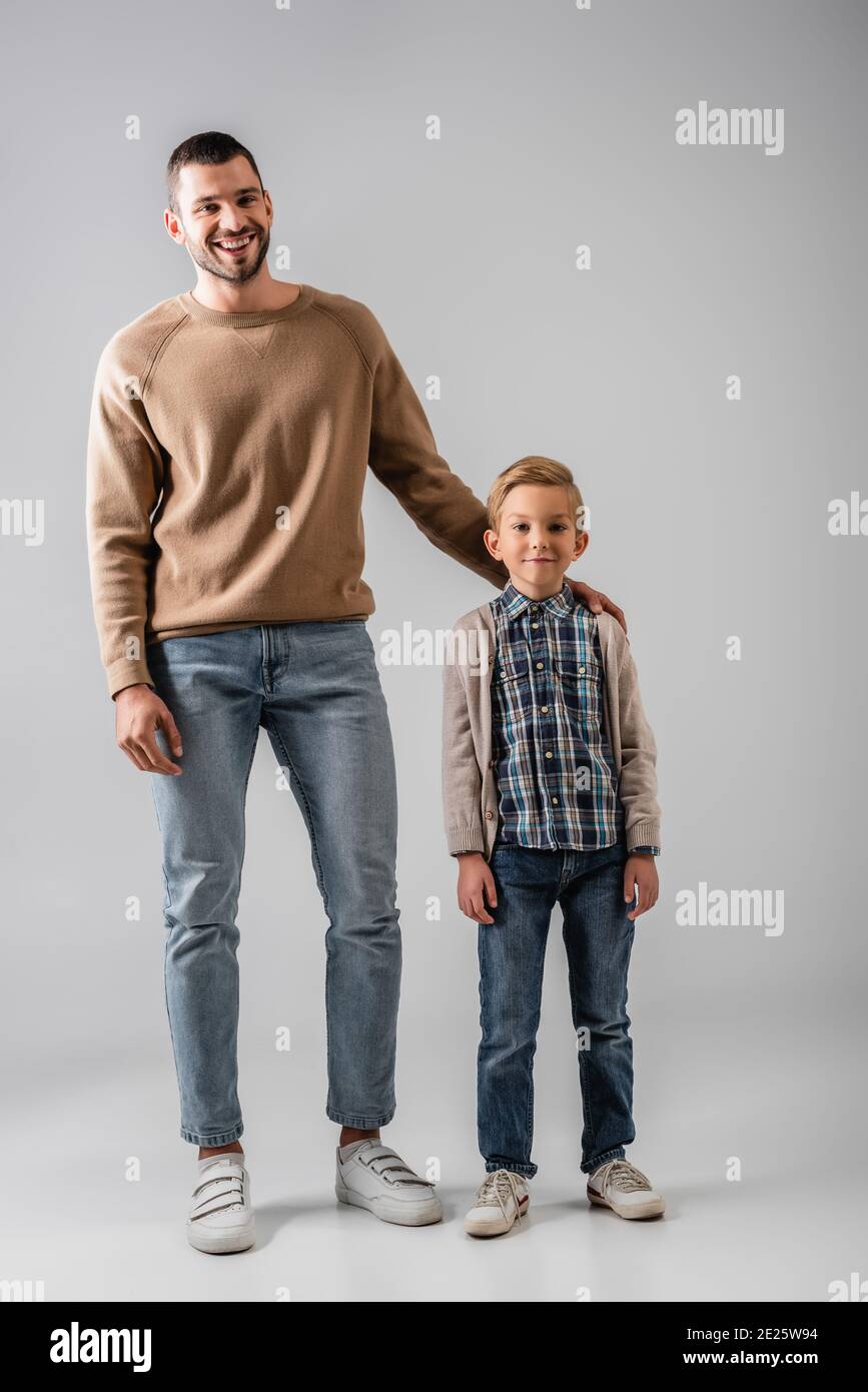 happy man hugging shoulder of son while standing together on grey Stock ...