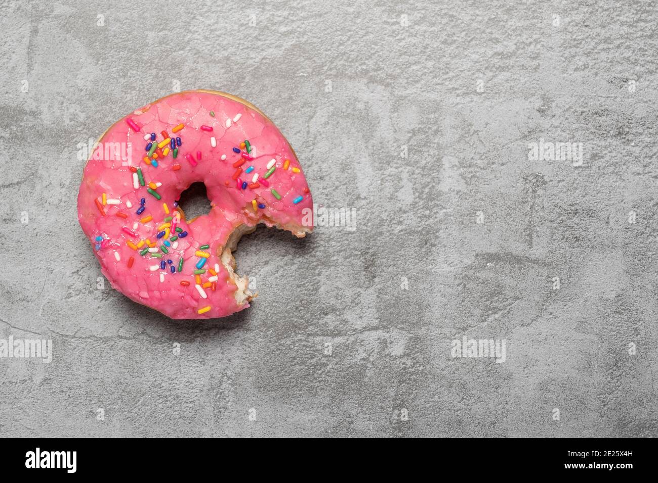 Partially eaten pink donut doughnut with sprinkles on a grey concrete ...