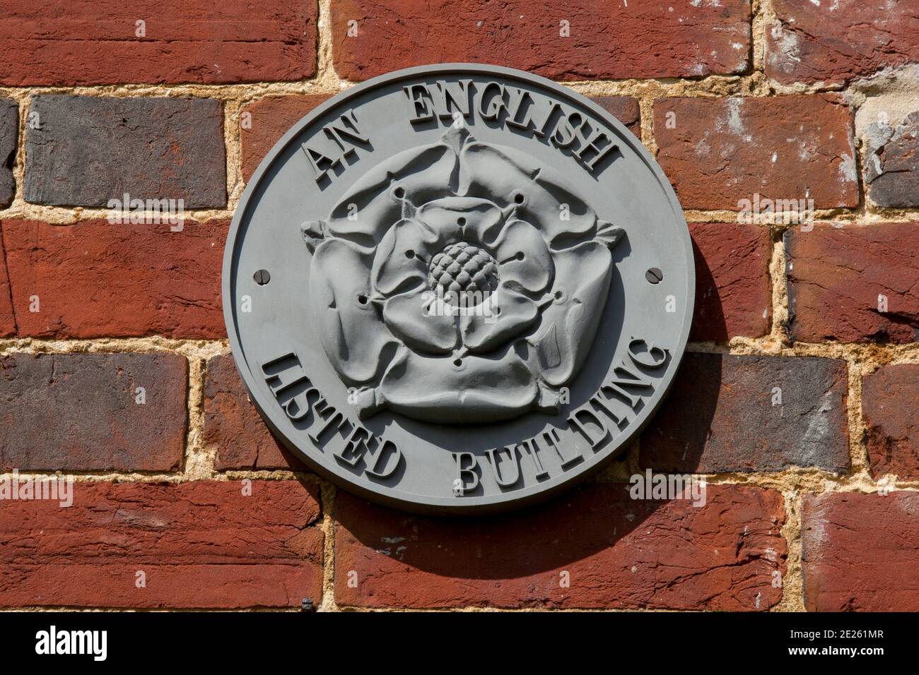 A round grey lead metal English Listed Building plaque on a red brick ...
