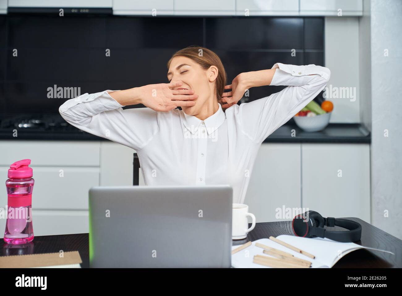 Tired young woman in casual clothing stretching and yawning while ...