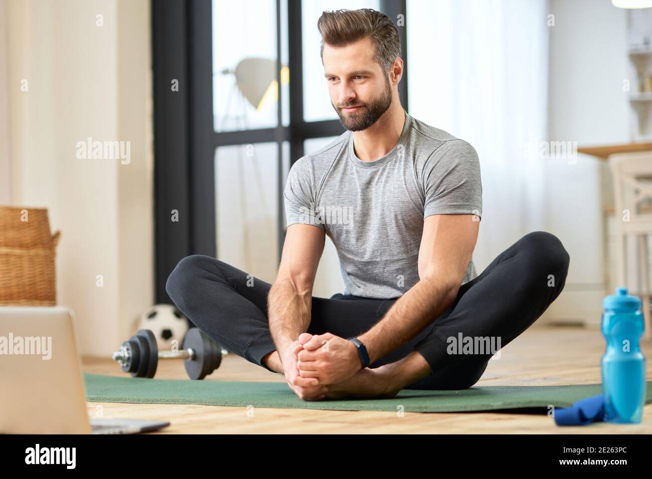 Bearded Athletic Gentleman Sitting On Yoga Mat And Watching Online
