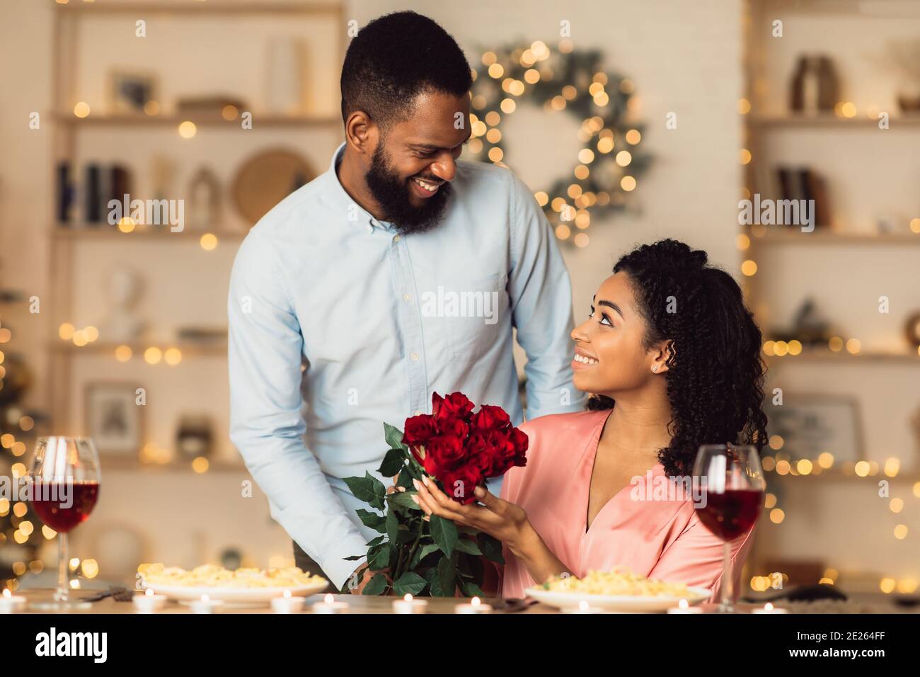 Smiling young black man giving red roses to woman Stock Photo - Alamy