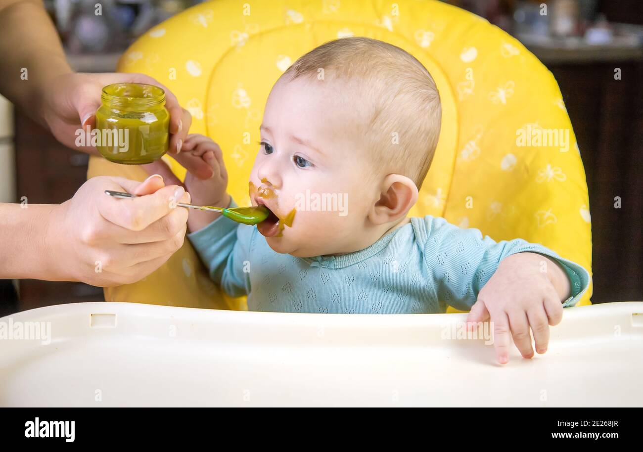 Little baby is eating broccoli vegetable puree. Selective focus. people ...