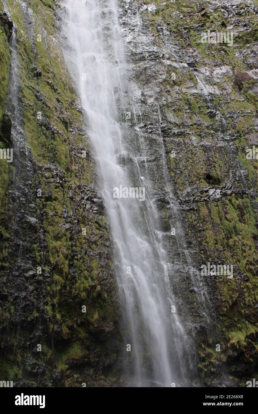 The bottom of Waimoku Falls streaming down a volcanic rock cliffside ...