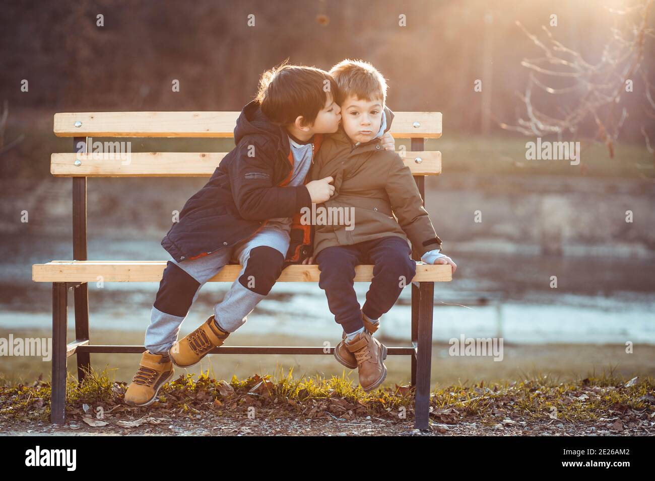 Two cute boys, brothers, sitting on a bench, being affectionate with ...