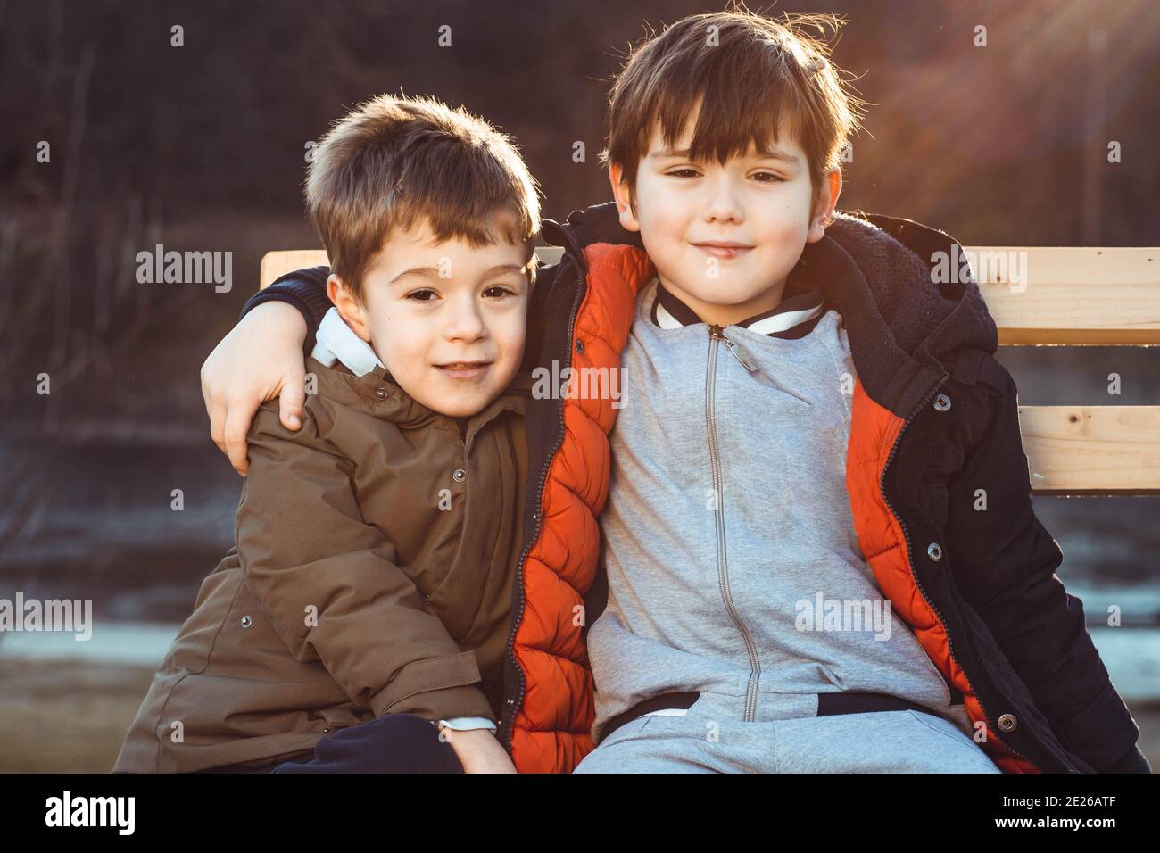 Two cute boys, brothers, sitting on a bench, being affectionate with ...