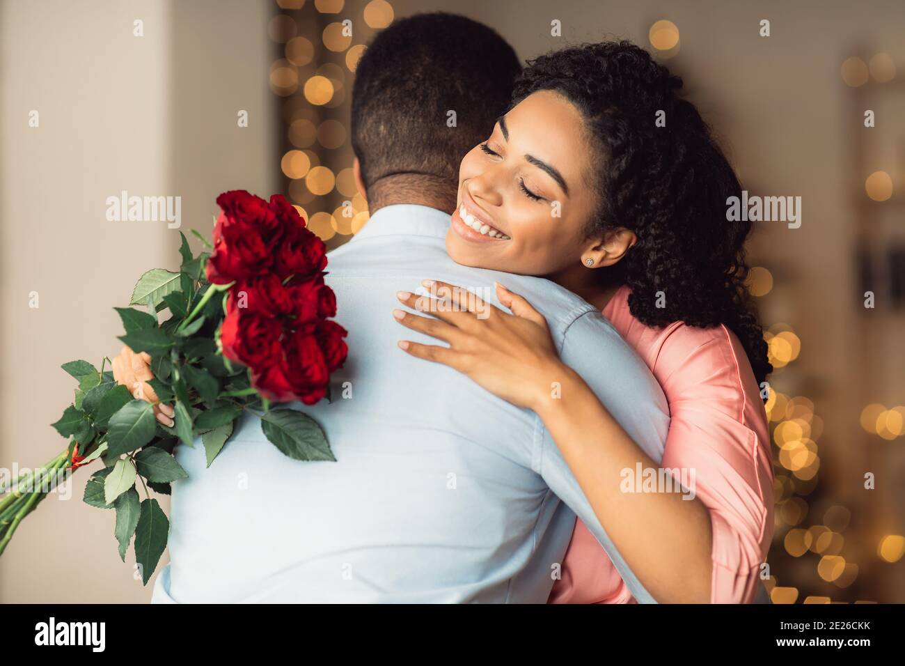Smiling young black woman hugging man holding red roses Stock Photo - Alamy
