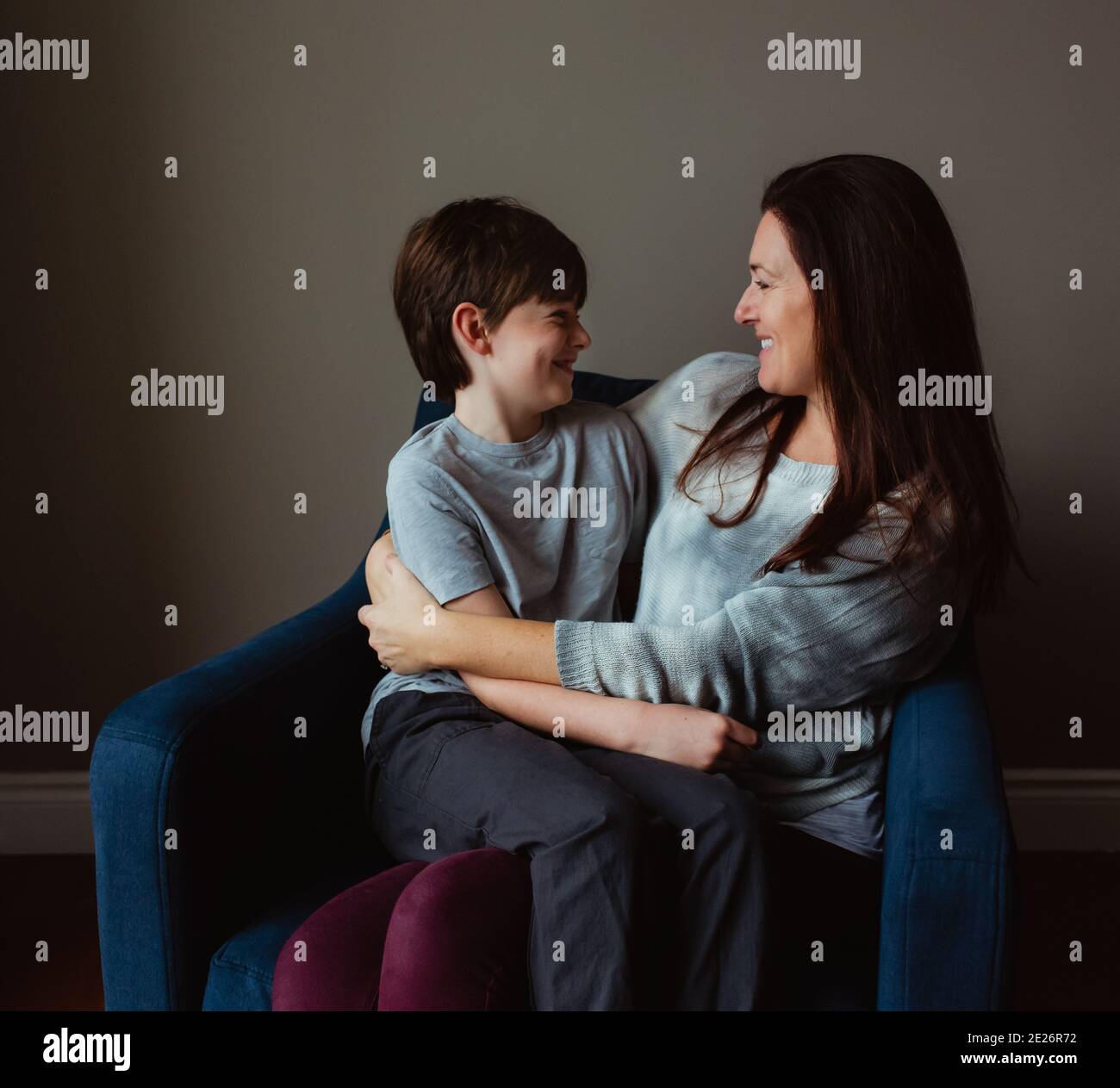 Happy woman hugging her smiling son as he sits in her lap on a chair ...