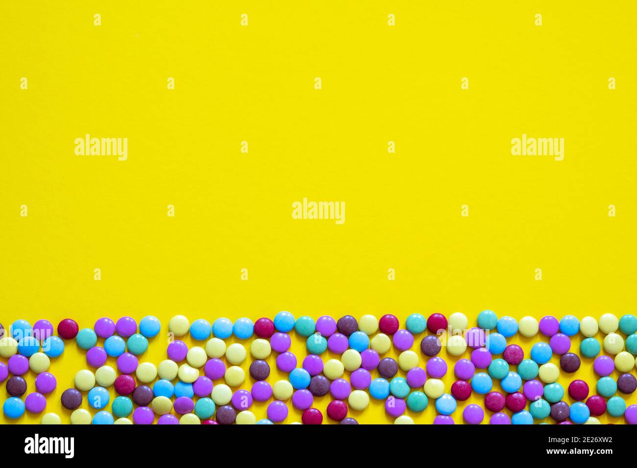 Colored candy border with sugar coated chocolate cuties on light blue ...