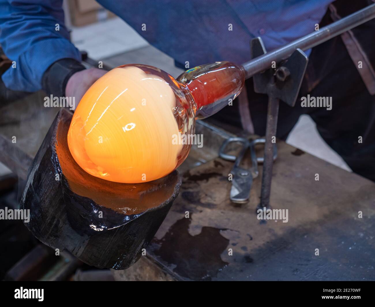 Glassblower is using wet wooden form for shaping the red melted glass ...