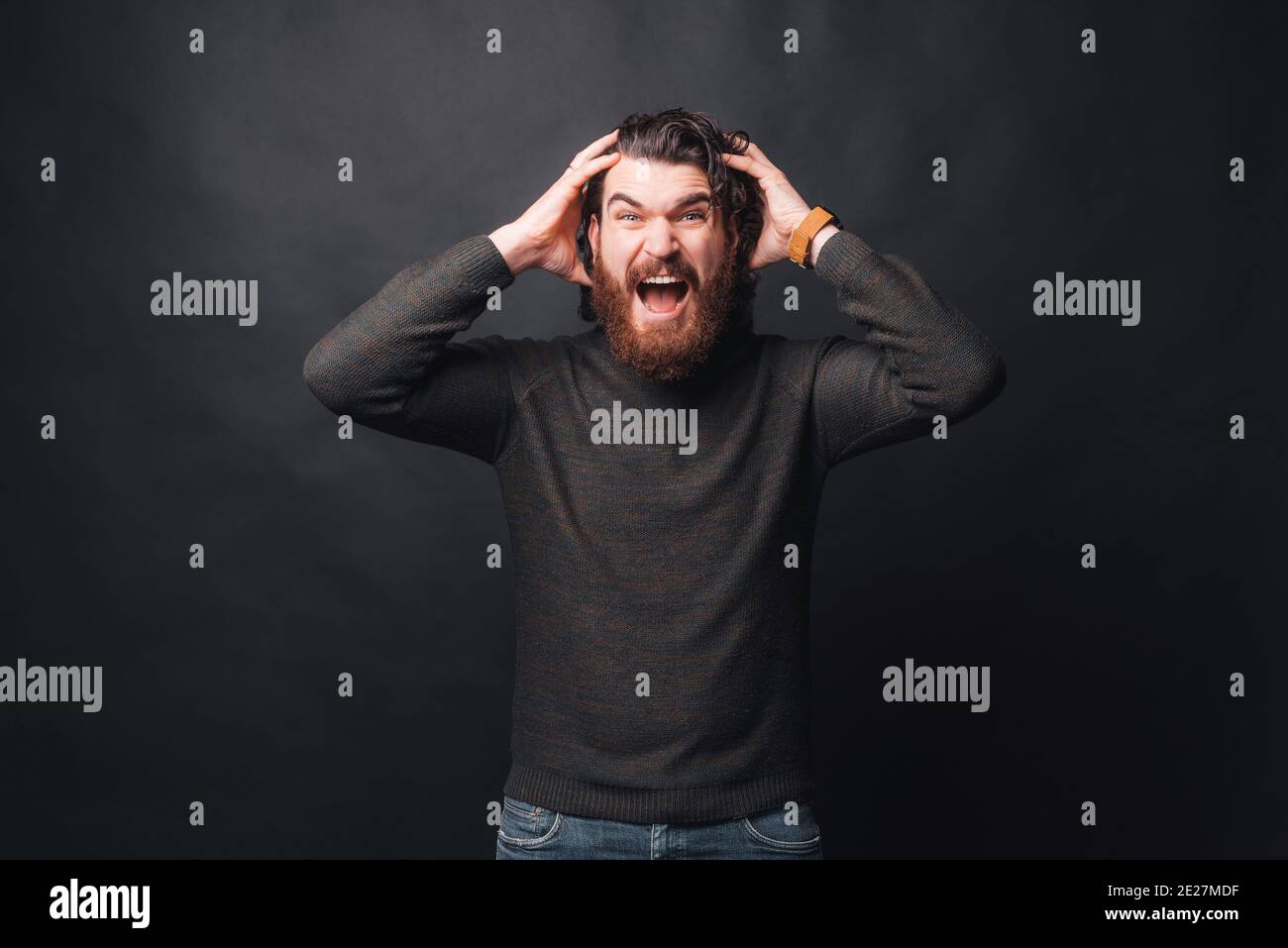 Photo of angry bearded man standing over dark background holding head ...