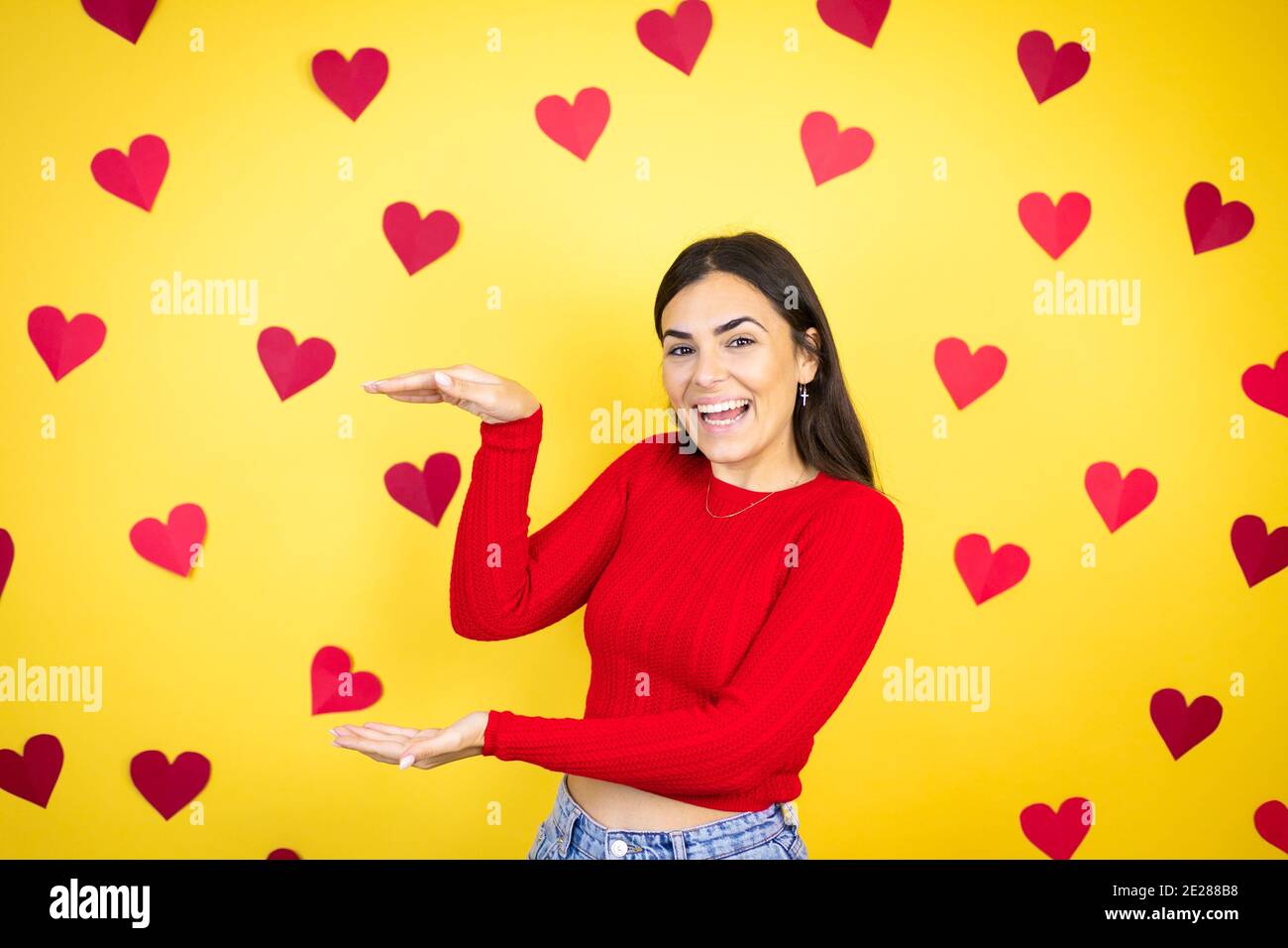 Young caucasian woman over yellow background with red hearts gesturing ...