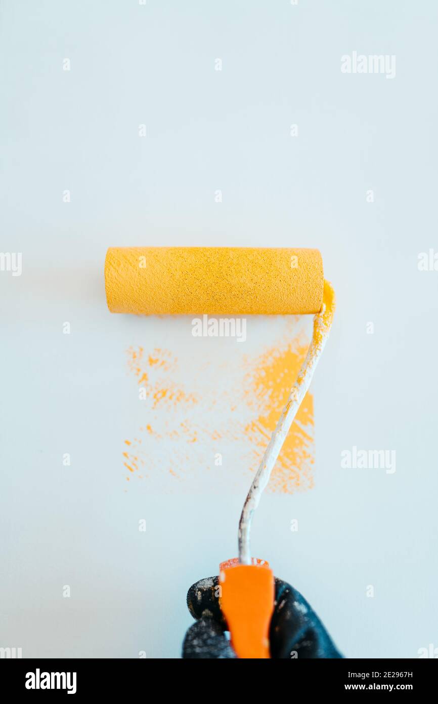 Hand painting roll with yellow paint over painted white background ...