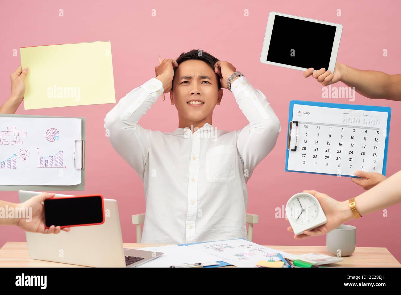 Sad young man sits at desktop, hands with papers, alarm clock, touchpad ...